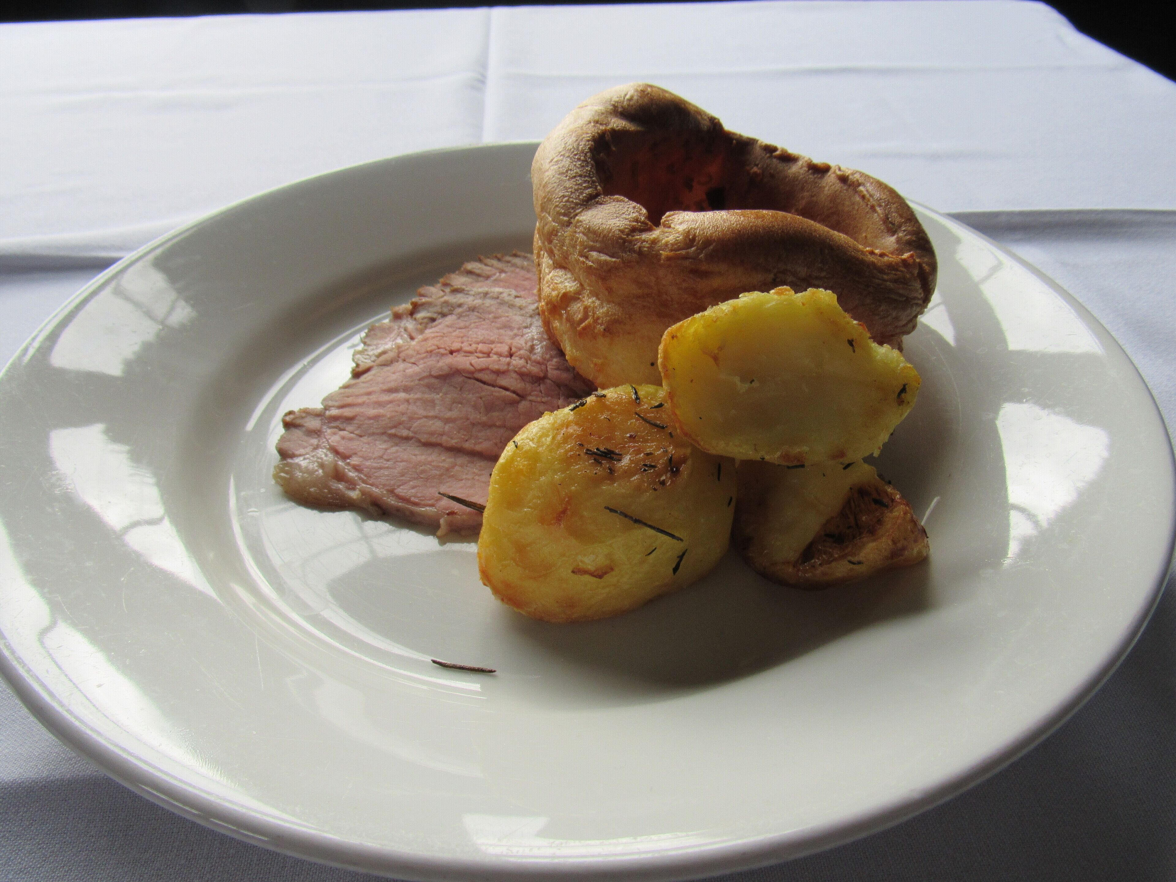 Prato com fatias de rosbife, pudim de Yorkshire e batatas assadas.