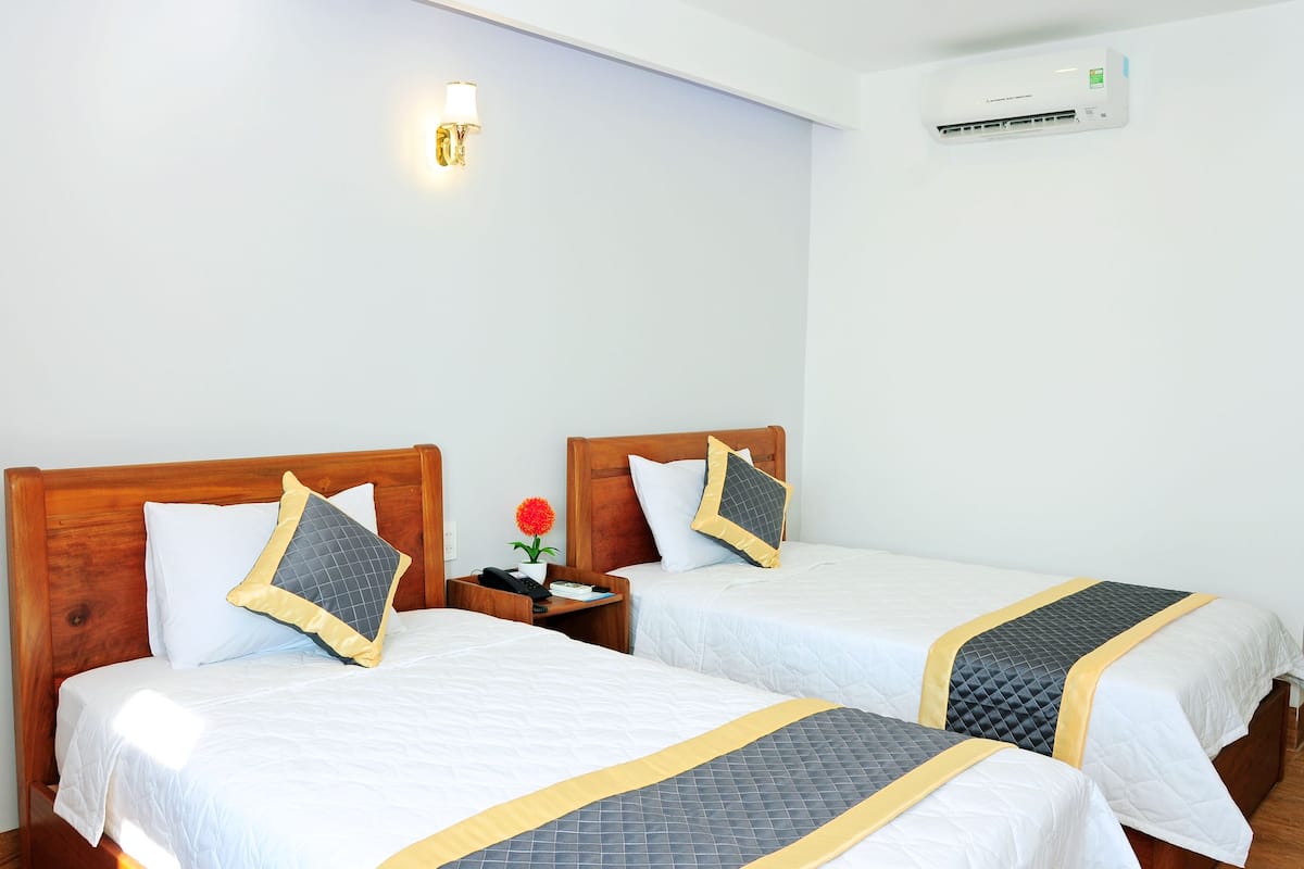 Quarto de hotel com duas camas, uma mesa de cabeceira, uma luminária e aparelho de ar condicionado.