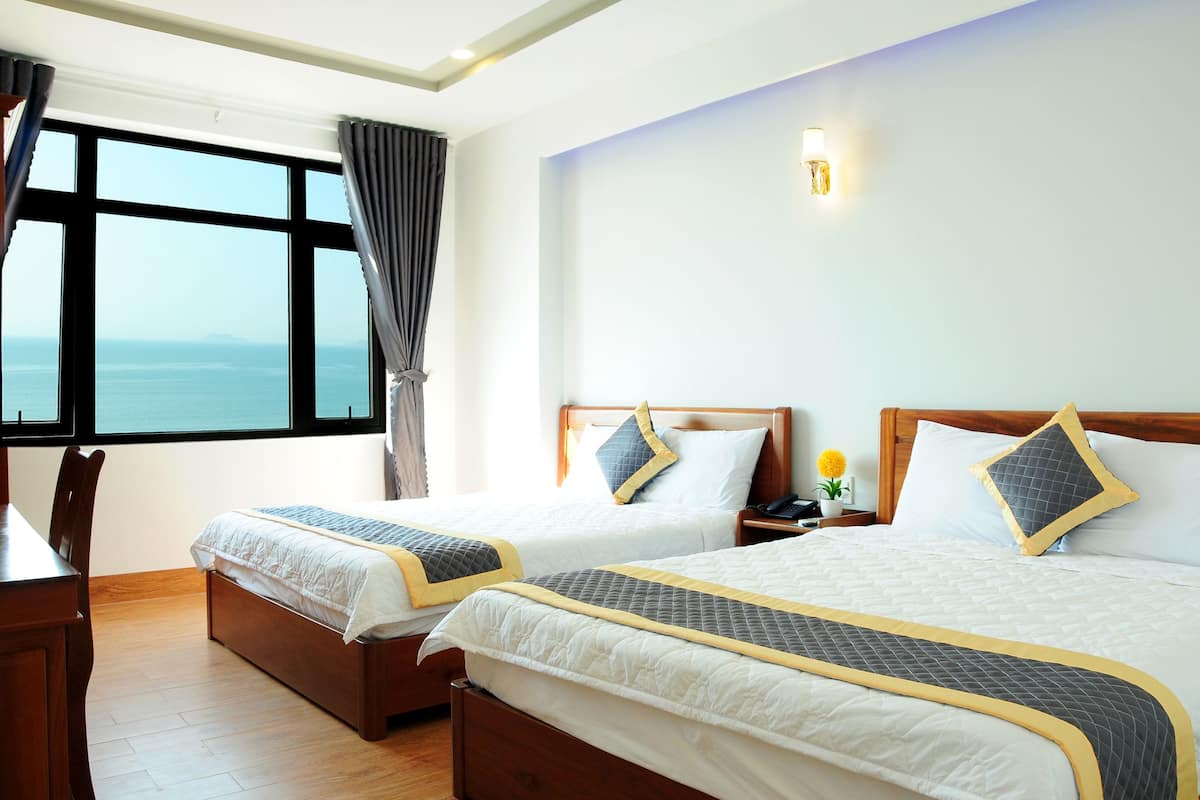 Quarto de hotel com duas camas, uma escrivaninha e vista para o mar.