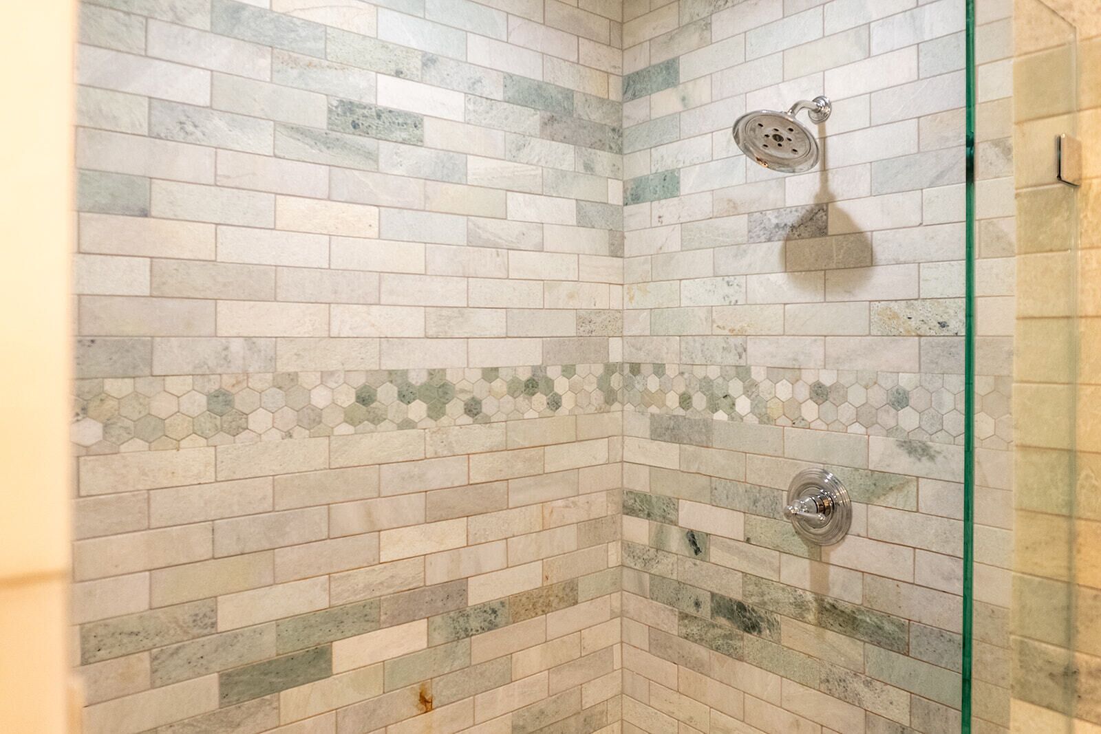 Chuveiro com parede revestida em azulejo e porta de vidro.