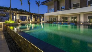 Um hotel moderno com piscina, espreguiçadeiras e uma área coberta com palmeiras.