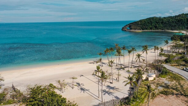 Uma praia com águas turquesa cristalinas, palmeiras e uma faixa de areia.