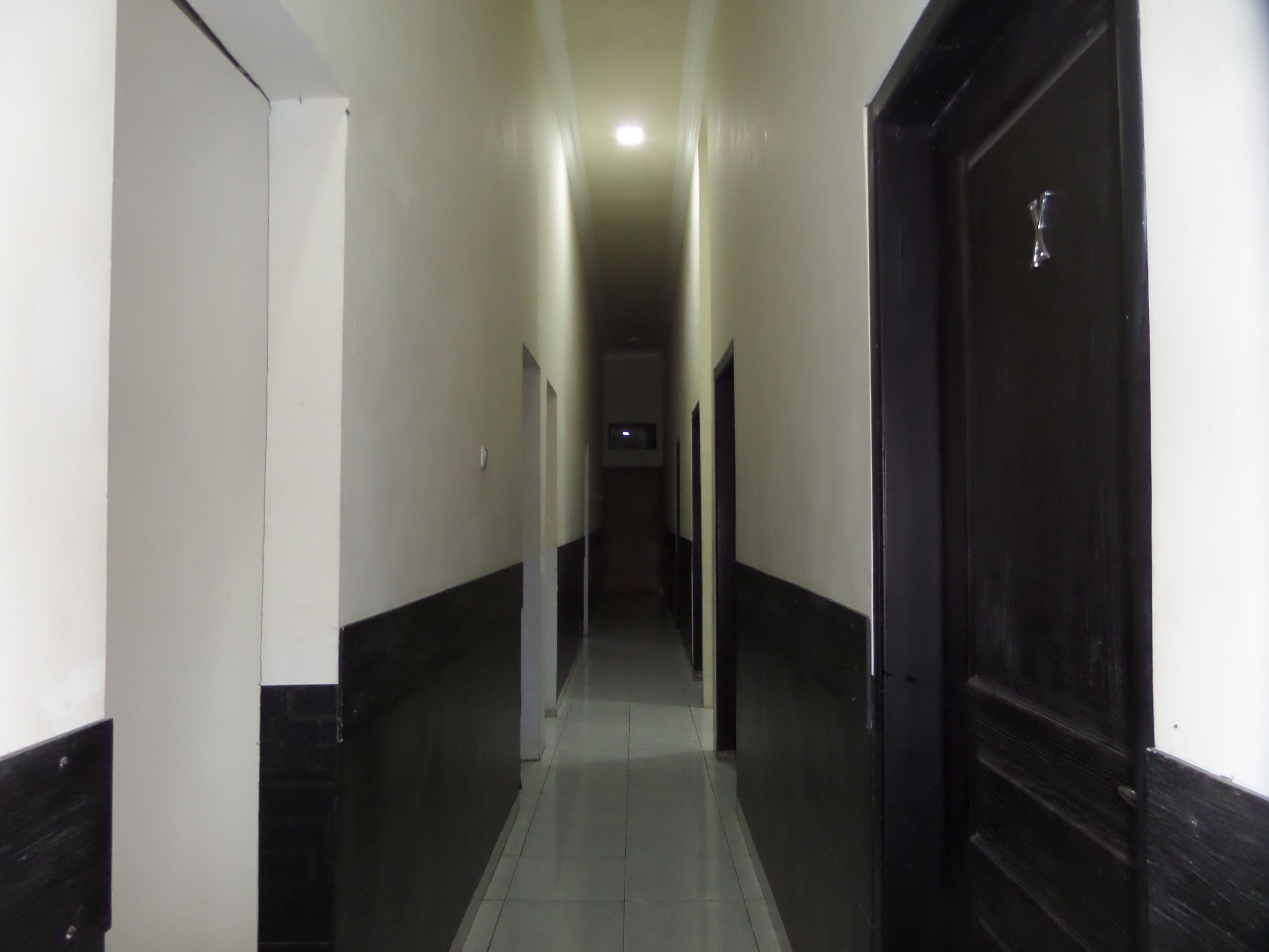 Um corredor com portas em ambos os lados, piso de azulejos e um luminário no teto.