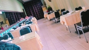 Uma sala de banquetes com mesas postas para refeições, cadeiras e um palco.