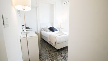 Quarto de hotel com cama, escrivaninha, luminária e cafeteira.