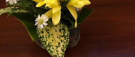 Uma mesa com um vaso de flores amarelas e uma chávena de líquido amarelo com fios vermelhos.