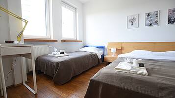 Quarto de hotel com duas camas, uma escrivaninha, uma luminária e obras de arte na parede.