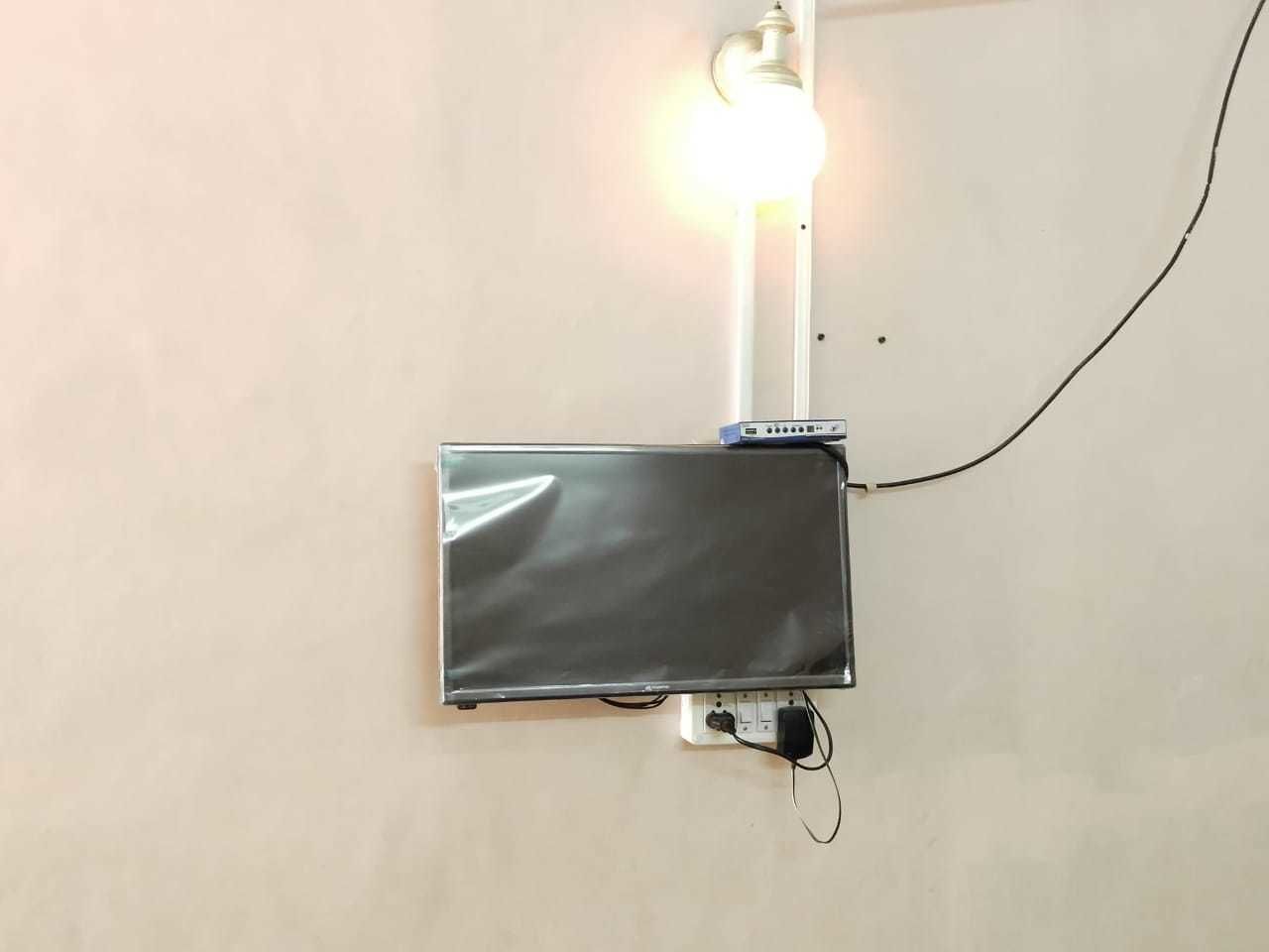 Televisão de tela plana fixada na parede, com régua de energia e um abajur.