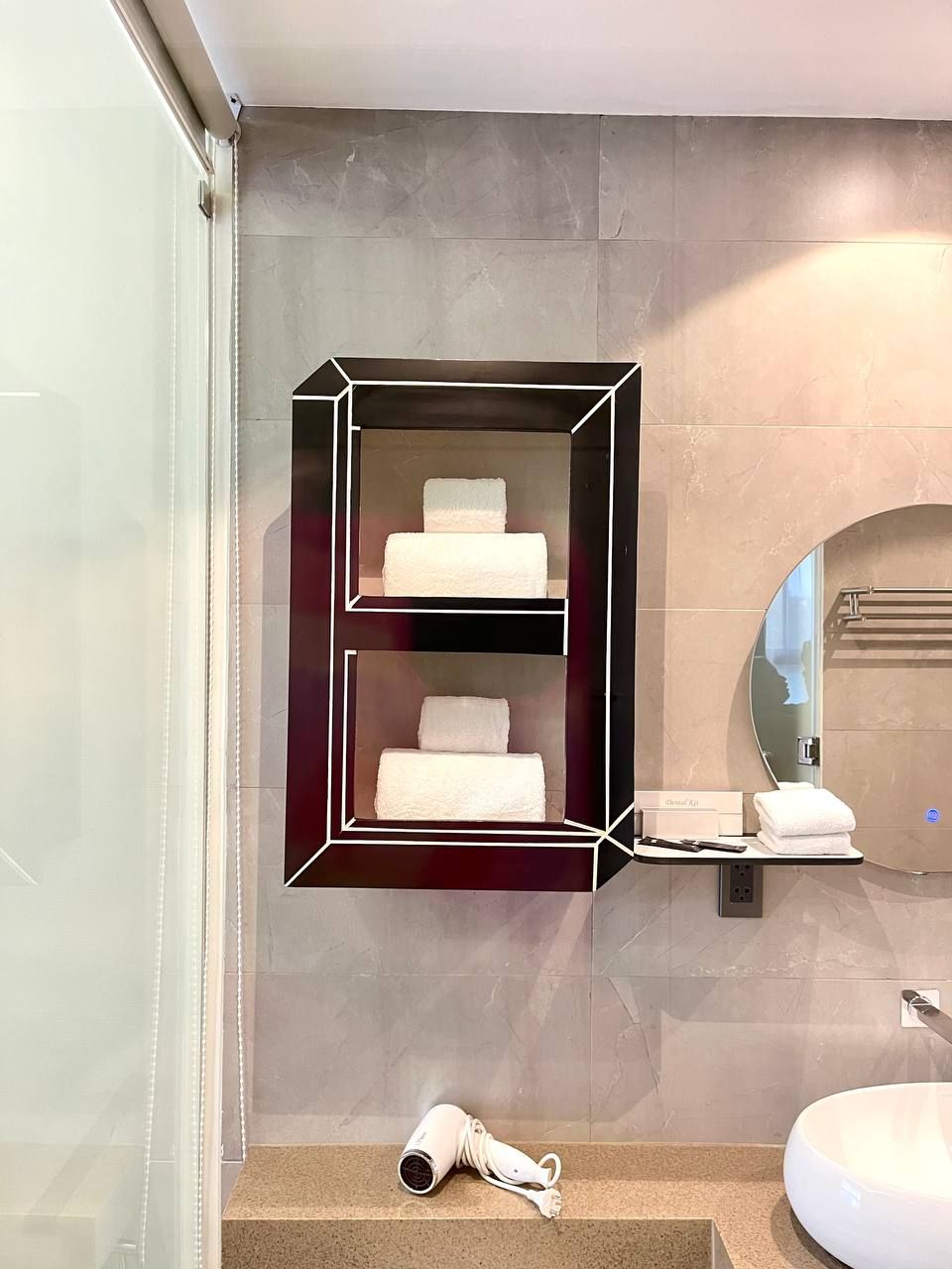 Casa de banho com prateleira embutida com toalhas, secador de cabelo na bancada e espelho.