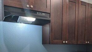Cozinha com armários de madeira escura, bancada branca e micro-ondas embutido.