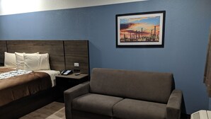 Quarto de hotel com uma cama, um sofá marrom, uma mesa de cabeceira com telefone e um quadro na parede.