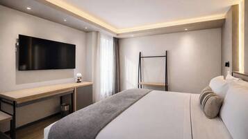 Quarto de hotel moderno com cama, escrivaninha, televisão de tela plana e mesa de cabeceira.