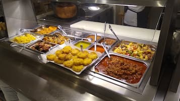 Buffet com diversos pratos, incluindo arroz amarelo, curry vermelho e outras opções variadas.
