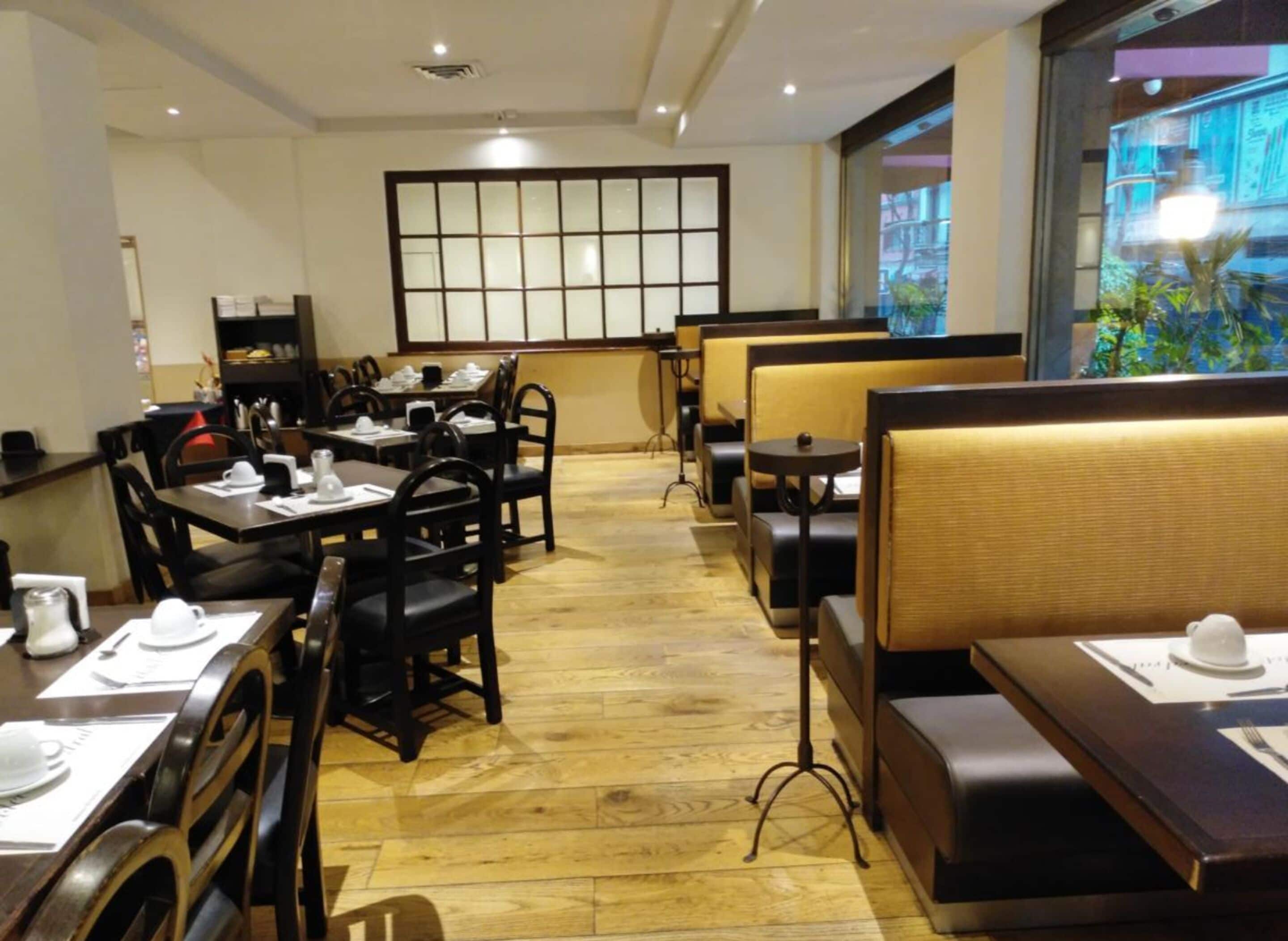 Interior de restaurante com piso de madeira, assentos em cabines pretas e amarelas, e mesas com louças brancas.