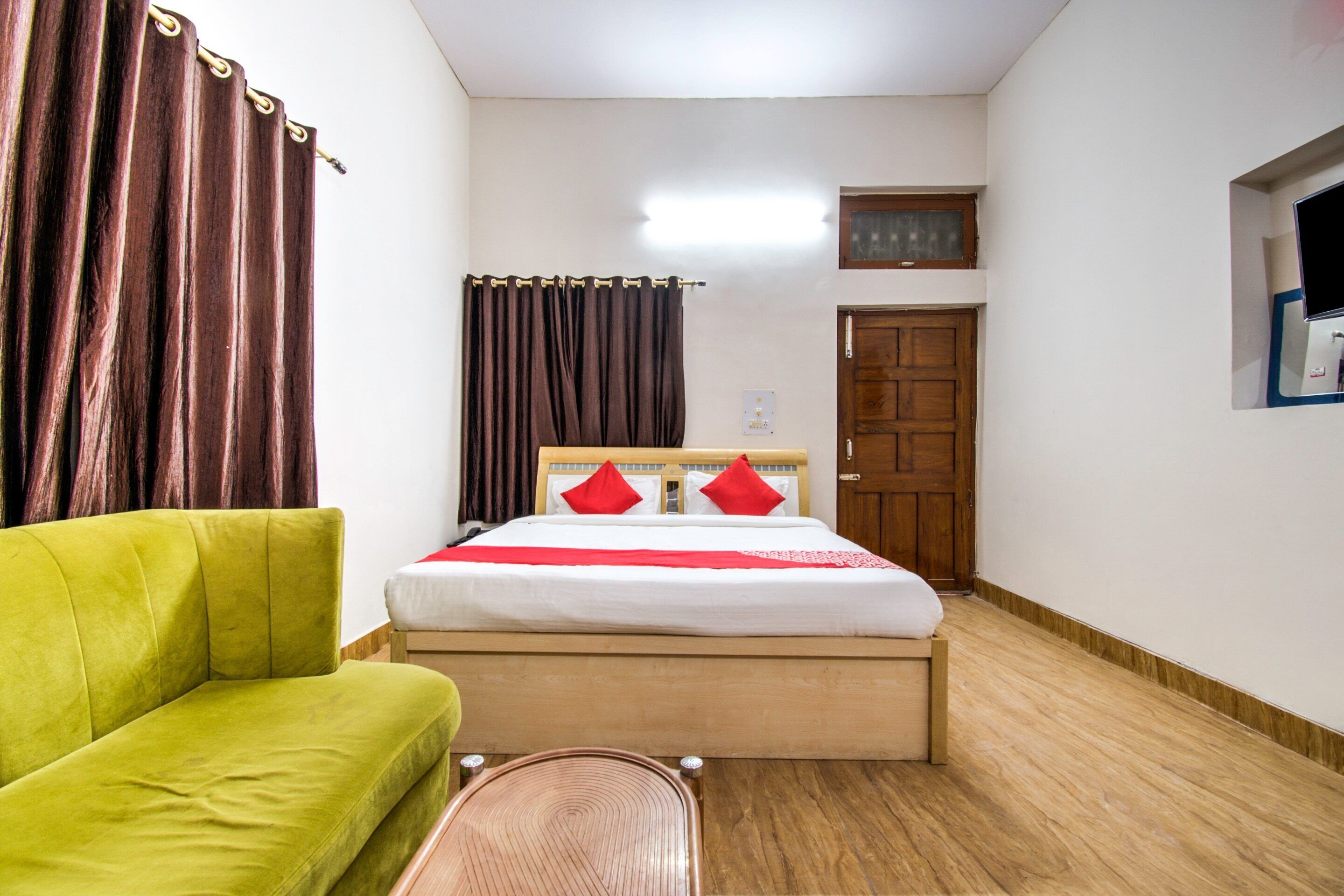Quarto de hotel com uma cama, um sofá verde, piso de madeira e porta de madeira.