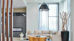 Uma sala de estar moderna com sofá modular, mesa de centro redonda, lareira e uma janela grande com cortinas.