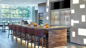 Uma área de bar moderna com balcão de madeira, banquetas e um refrigerador para bebidas.