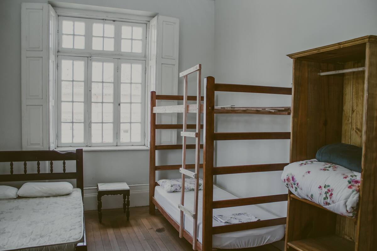 Um quarto com uma cama de solteiro, uma cama individual, um armário de madeira e uma janela com persianas.