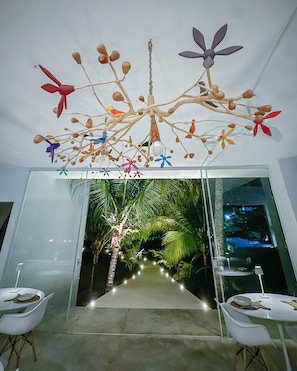 Um interior moderno com um design de teto único, uma porta de vidro que dá para uma área externa tropical e uma mesa de jantar com cadeiras.