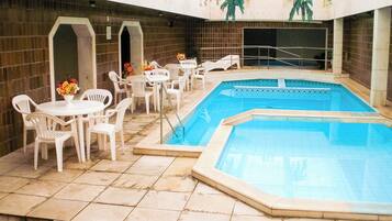 Piscina interna com revestimento de azulejos, cadeiras e mesas de plástico branco.