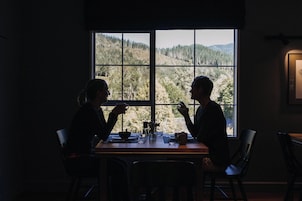 Duas pessoas sentadas à mesa com vista para uma floresta através de uma janela.