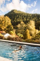 Piscina com uma pessoa na água, rodeada por árvores e uma montanha ao fundo.
