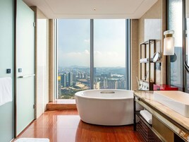 Um banheiro moderno com uma banheira grande, uma pia com espelho e vista para o horizonte urbano através de amplas janelas.