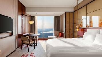 Quarto de hotel com uma cama grande, uma escrivaninha com cadeira, televisão e vista para a cidade.