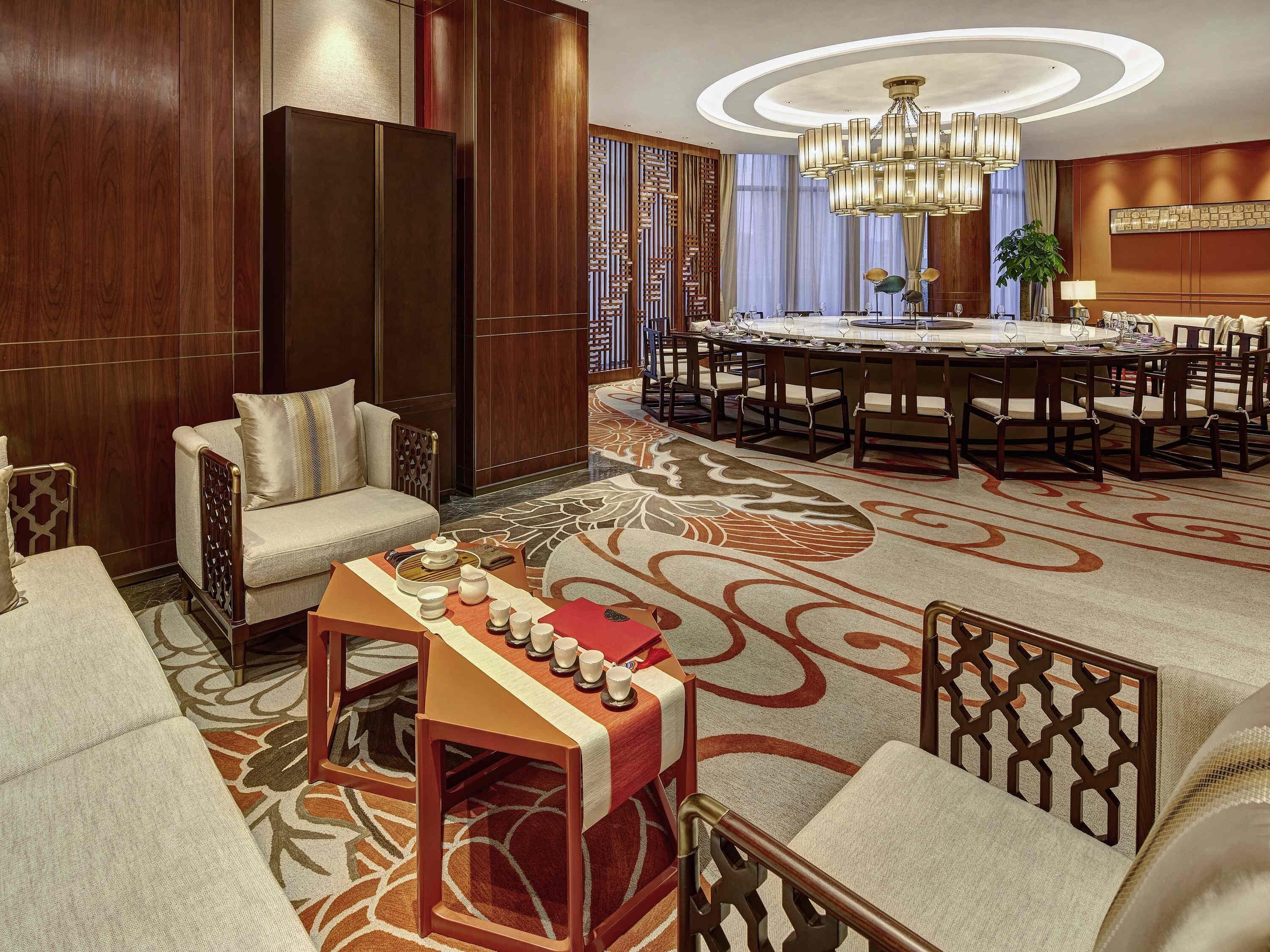 Quarto de hotel com área de jantar, sofá, mesa pequena com bules e tapete decorativo.