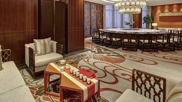 Quarto de hotel com área de jantar, sofá, mesa pequena com bules e tapete decorativo.