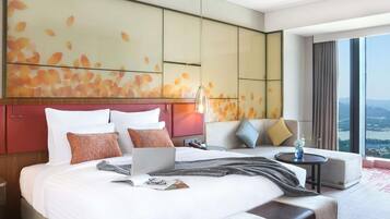 Quarto de hotel moderno com uma cama grande, área de estar e vista para um lago.