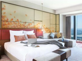 Quarto de hotel moderno com uma cama grande, área de estar e vista para um lago.