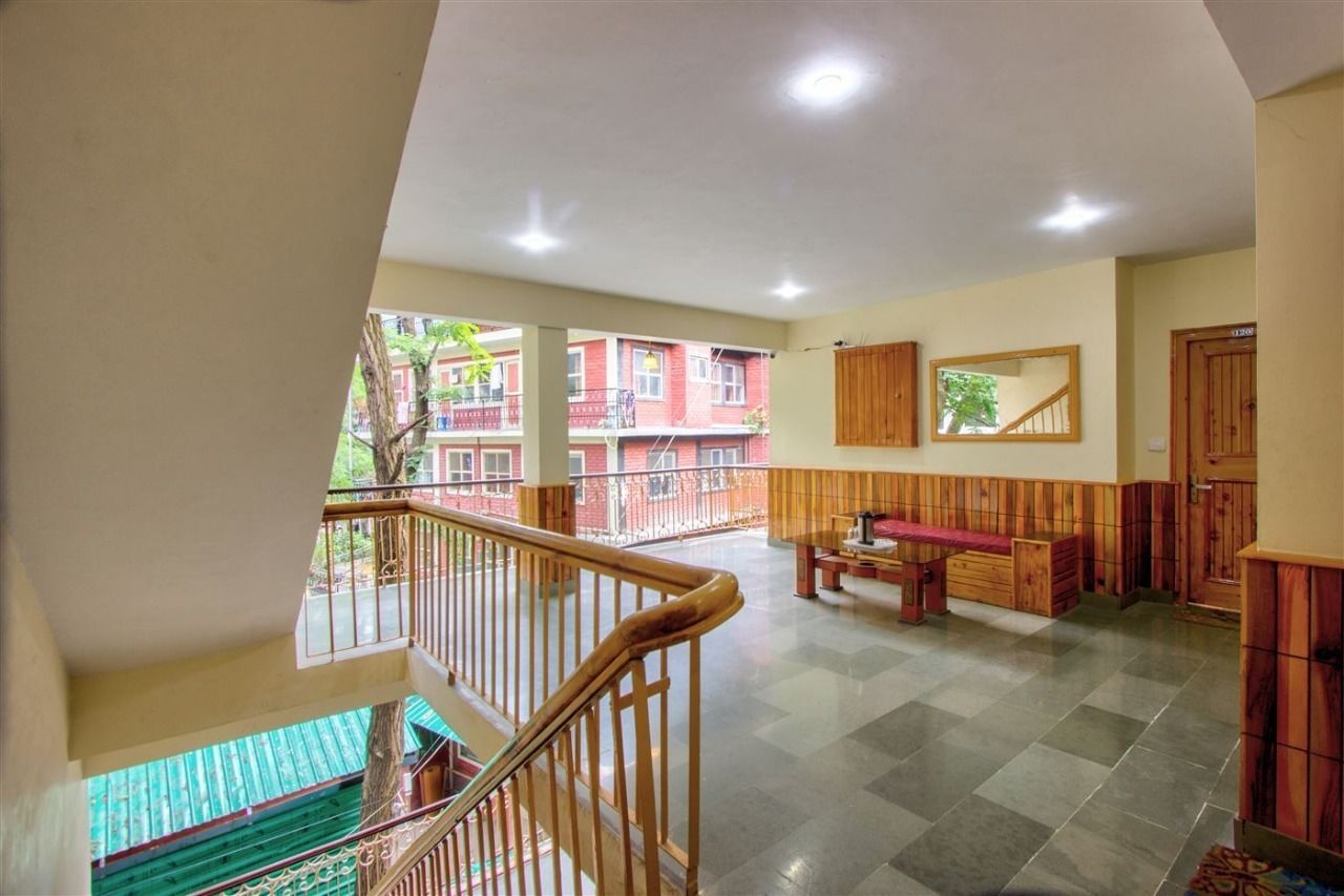 Amplo espaço interno com um banco de madeira, uma escada e vista para um edifício vermelho lá fora.