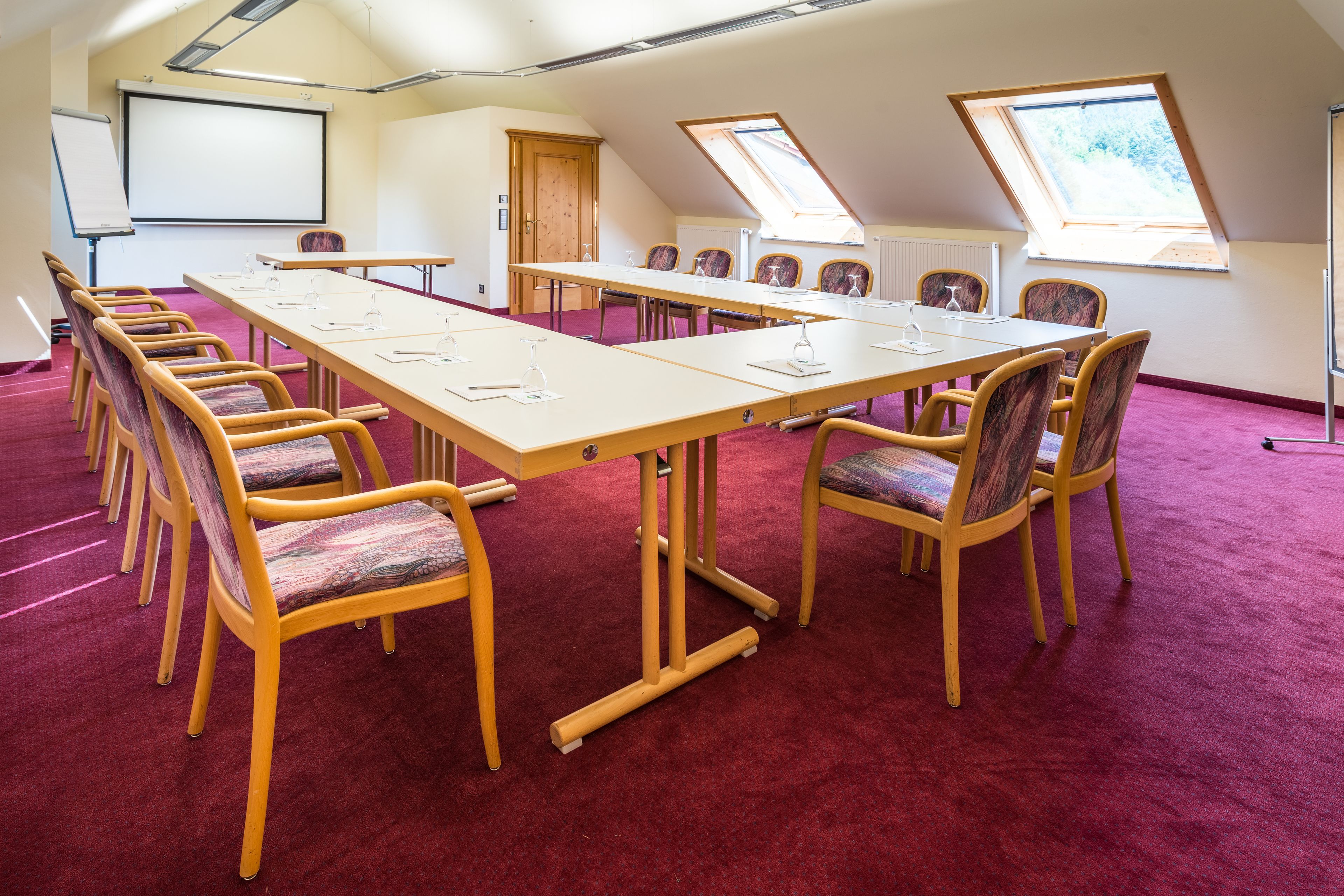 Uma sala de conferências com uma mesa comprida, cadeiras, tela de projetor e claraboias.