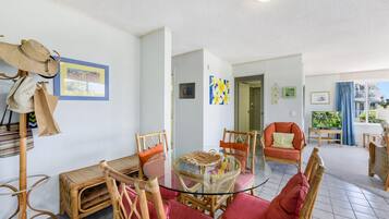 Uma sala de estar ampla com móveis de vime, uma mesa de centro de vidro e vista para uma varanda.