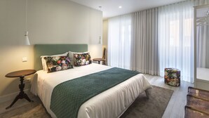 Quarto com uma cama, um edredom verde, uma mesa redonda e uma cadeira.