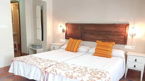 Uma cama de casal com colcha estampada, duas mesas de cabeceira, cabeceira de madeira e luminárias fixadas na parede.