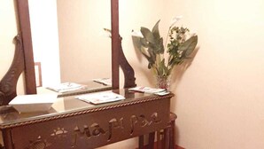 Uma casa de banho com toucador de madeira, um espelho, uma planta em vaso e uma toalha no chão.