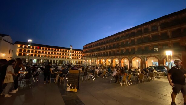 Uma praça movimentada com um edifício histórico com arcos e uma varanda.