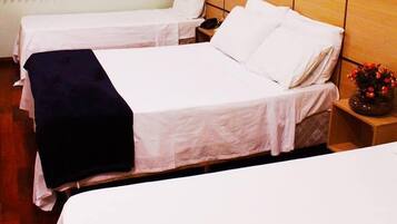 Quarto de hotel com duas camas de solteiro, cabeceira de madeira, mesa de cabeceira com um vaso de flores e janela com persianas.
