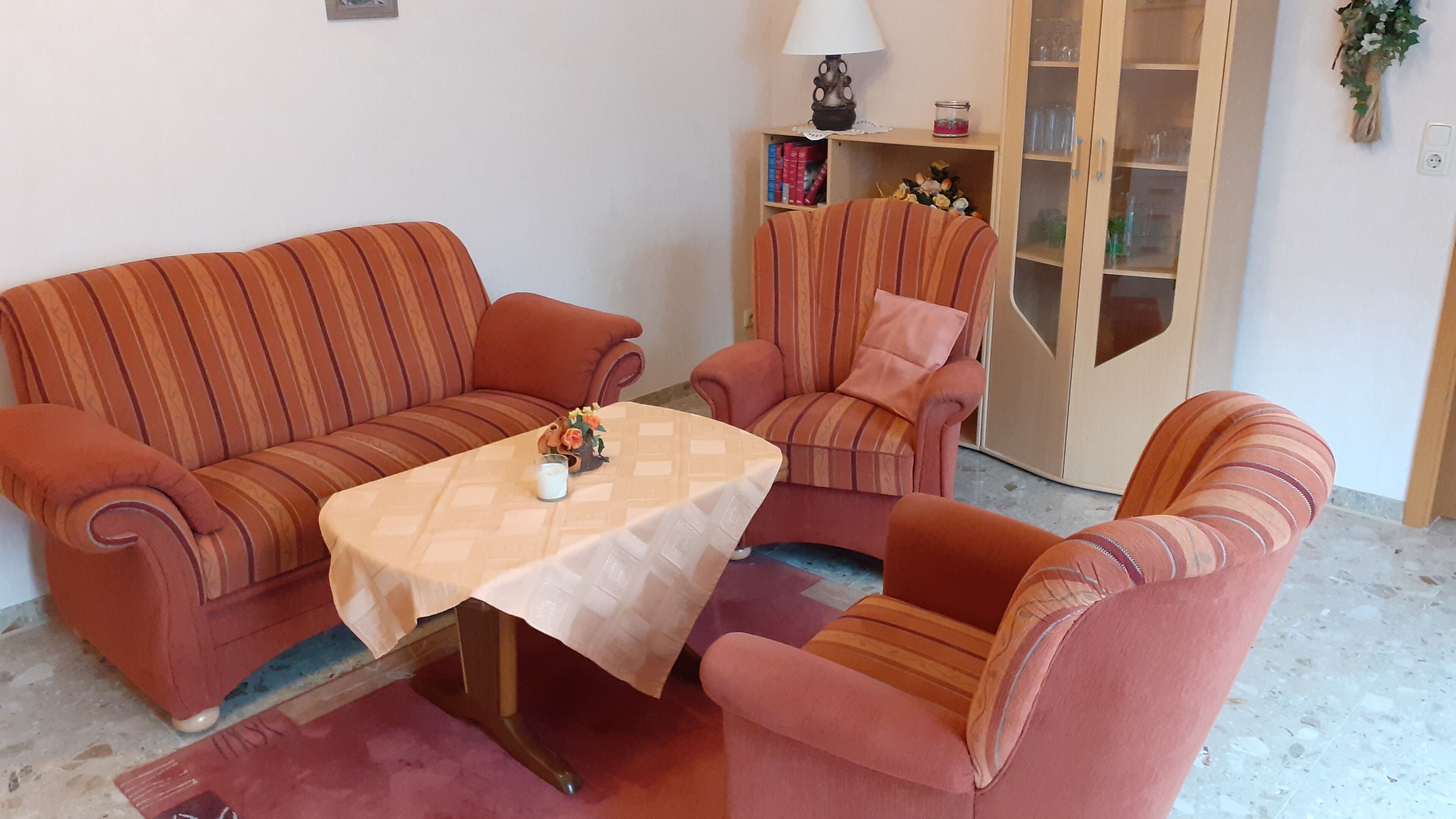 Uma sala de estar com um sofá, duas poltronas, uma mesinha e um armário.