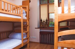 Quarto com beliche de madeira, uma prateleira pequena com um relógio e janela com vista para o verde.