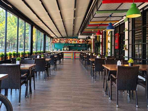 Restaurante com balcão comprido, cadeiras de vime e plantas em vasos.