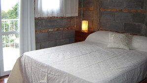 Um quarto com cama, mesa de cabeceira com luminária, janela com cortinas e parede de tijolos.