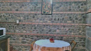 Paredes de pedra com um quadro emoldurado, uma mesa redonda com toalha branca e um cesto de flores.