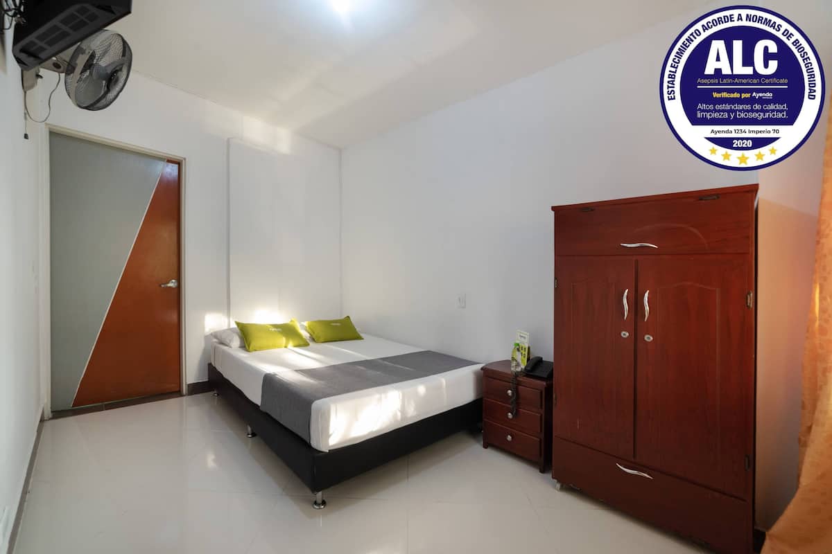Quarto de hotel com cama, guarda-roupa e escrivaninha com luminária.