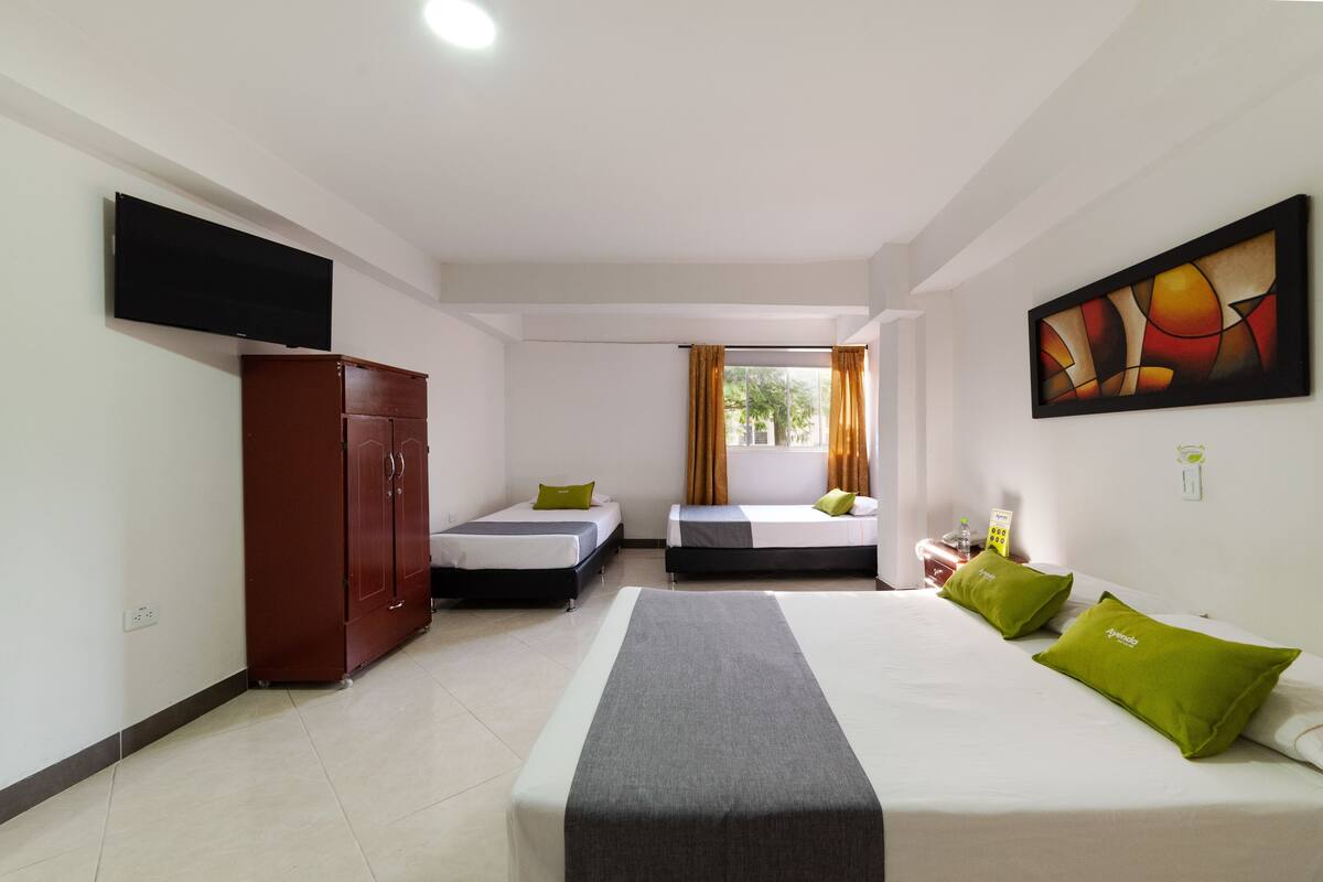 Quarto de hotel com duas camas, um guarda-roupa, uma televisão e um quadro na parede.