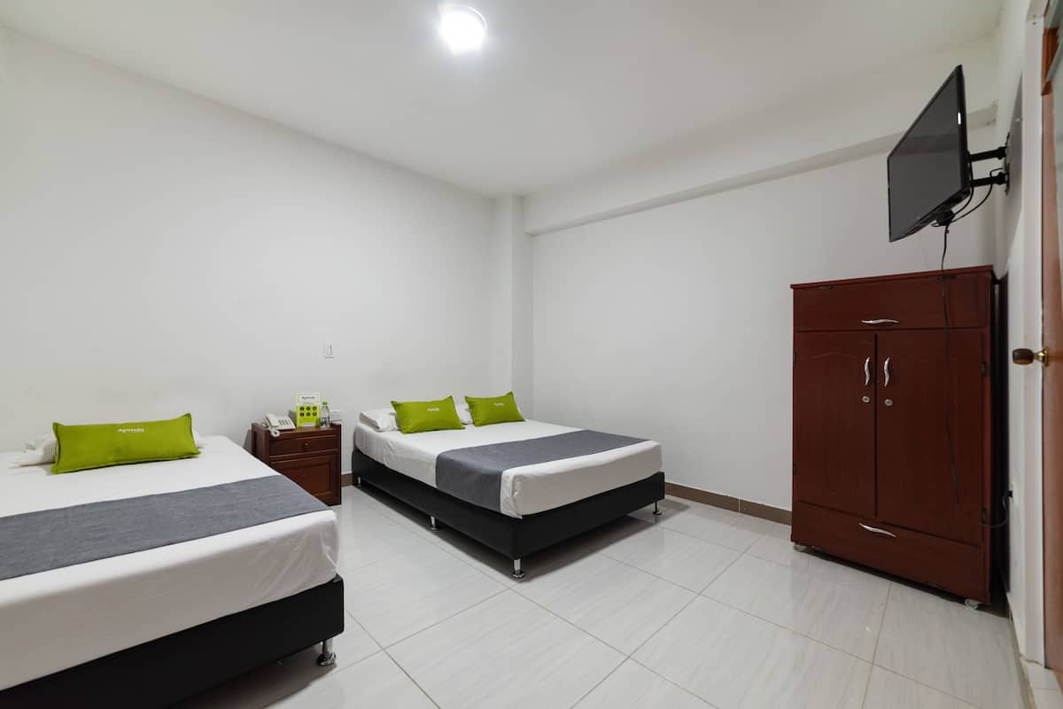 Quarto de hotel com duas camas, um guarda-roupa, uma TV e uma mesa de cabeceira com telefone e garrafa.