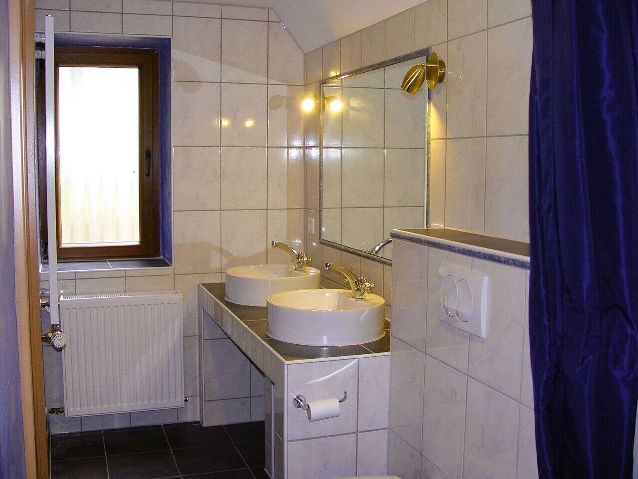Uma casa de banho com duas pias, um espelho, uma janela e um porta-toalhas.