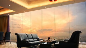 Sala de estar moderna com uma janela ampla, um sofá de couro preto, uma mesa de centro e vista para o horizonte da cidade.